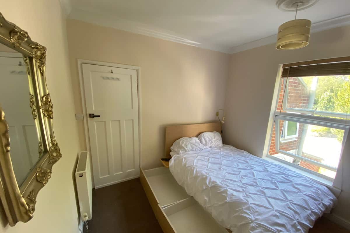 Quarto com cama, janela, porta e espelho.