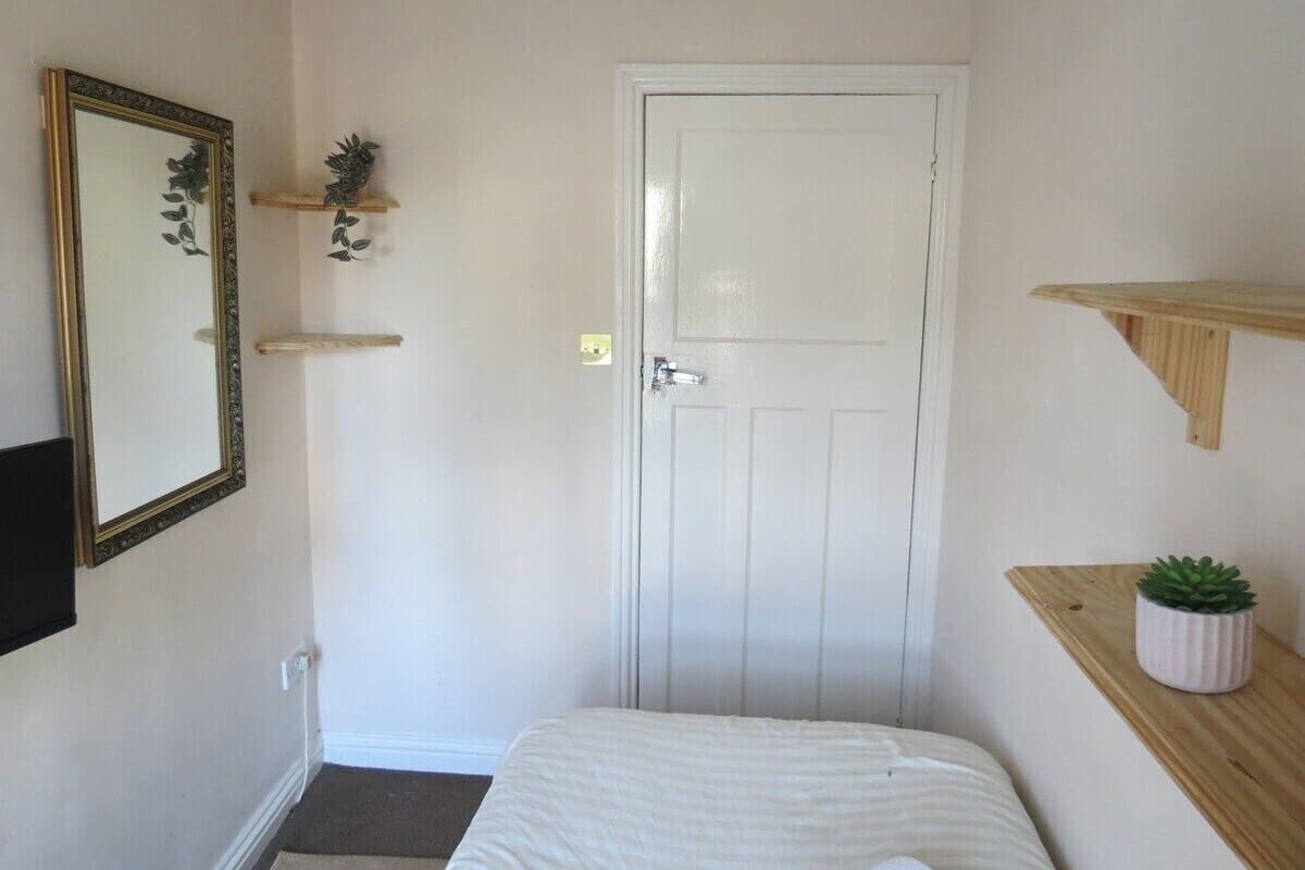 Quarto pequeno e bem arrumado com uma cama de solteiro, uma porta branca e um espelho na parede.