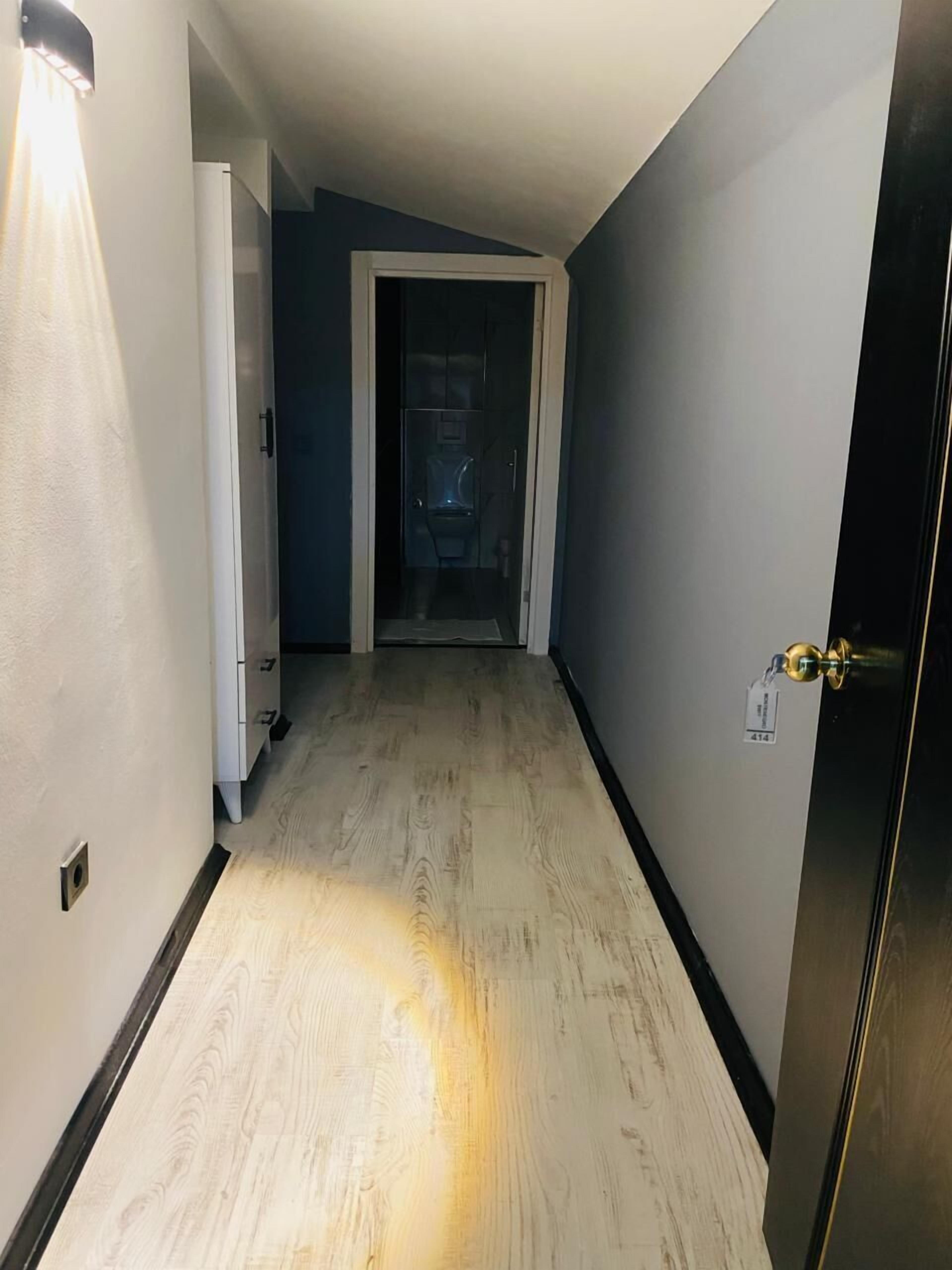 Um corredor com piso de madeira, uma porta à direita e uma porta branca à esquerda.