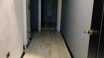 Um corredor com piso de madeira, uma porta à direita e uma porta branca à esquerda.