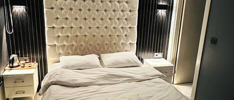 Quarto de hotel com uma cama grande, cabeceira, mesa de cabeceira com abajur e ar condicionado.