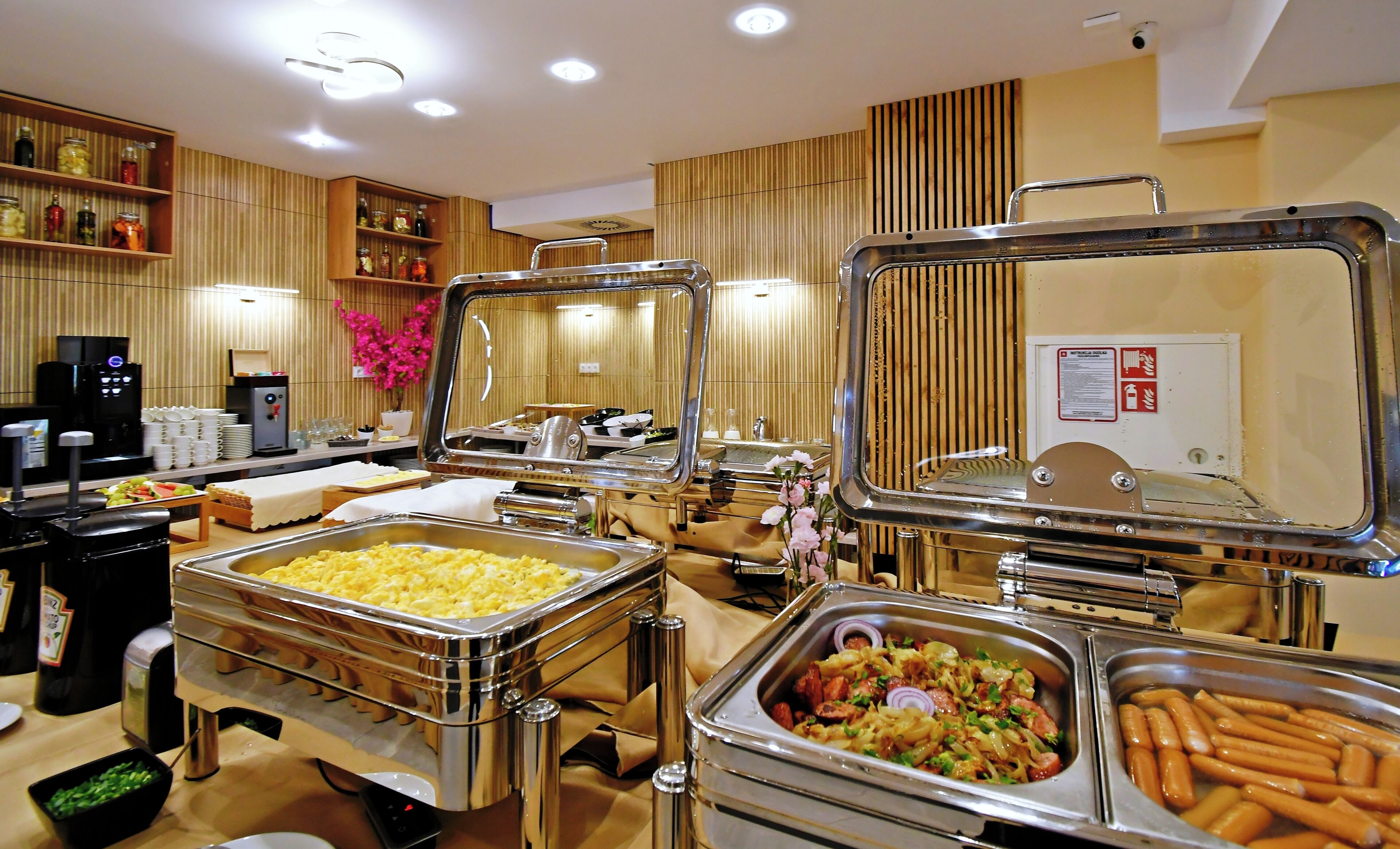 Uma mesa de buffet com diversas opções de comida, uma máquina de café e uma planta decorativa.