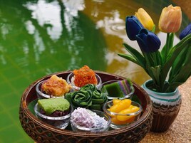 Uma bandeja com sobremesas coloridas, uma tigela decorativa, um vaso com tulipas e um lago ao fundo.