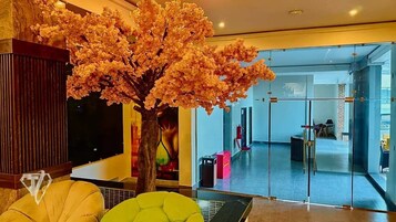 Um saguão com uma grande cerejeira artificial, uma mesa de recepção e um painel de vidro.
