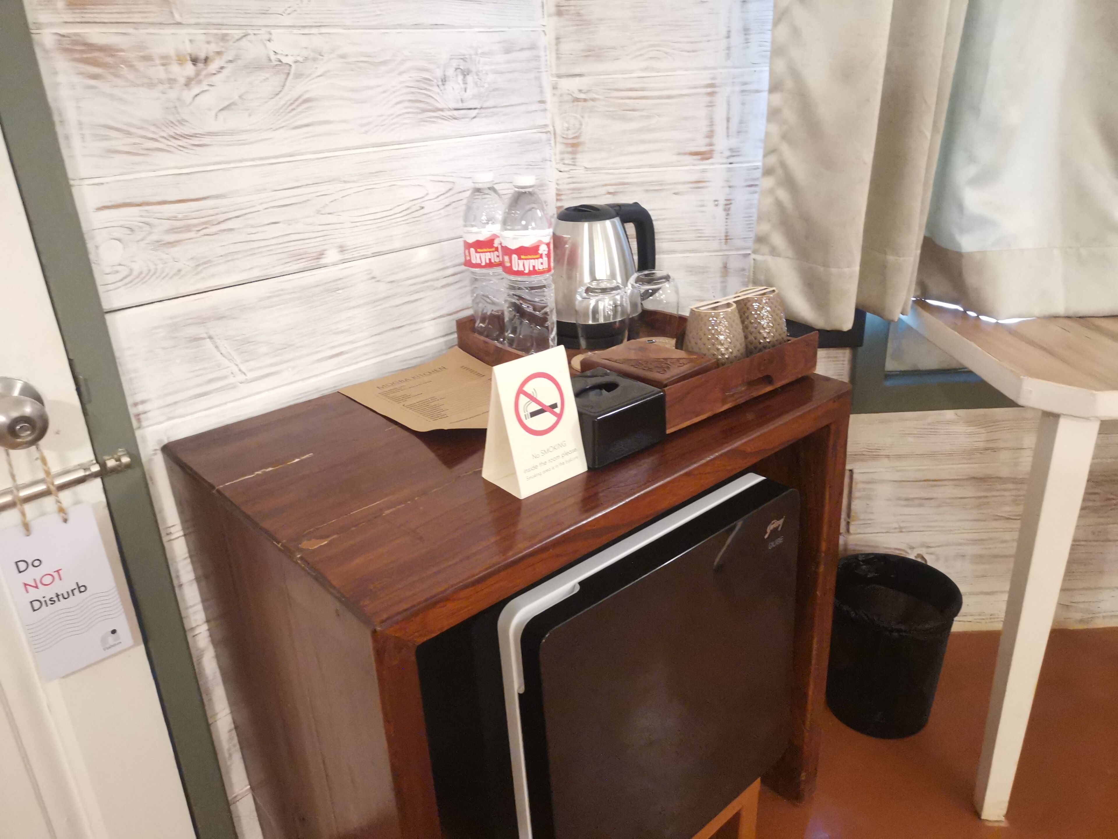 Uma pequena cozinha compacta com cafeteira, garrafas de água e um suporte com copos e caixa de lenços.