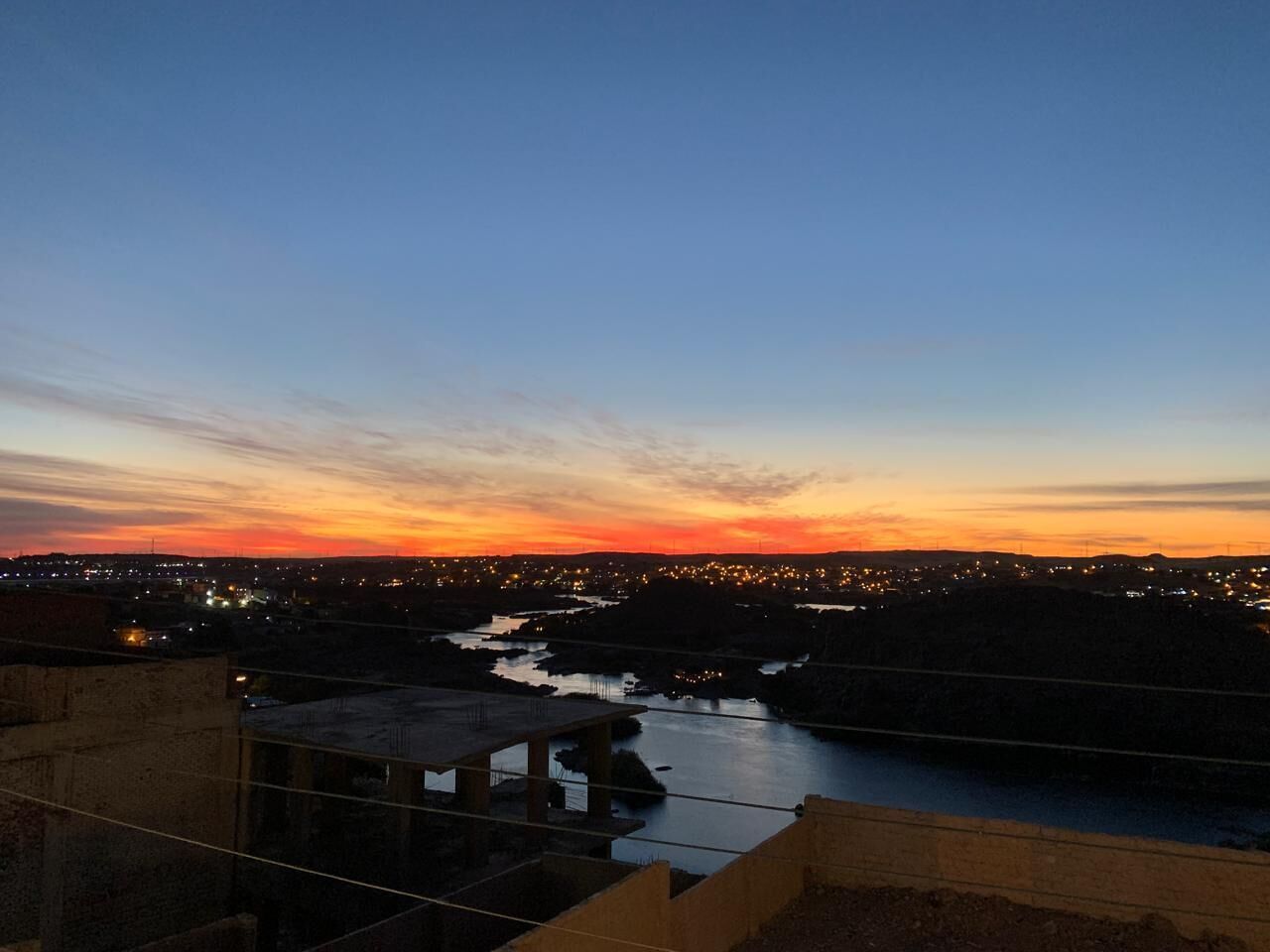 Vista do pôr do sol sobre um rio, com edifícios ao longe.