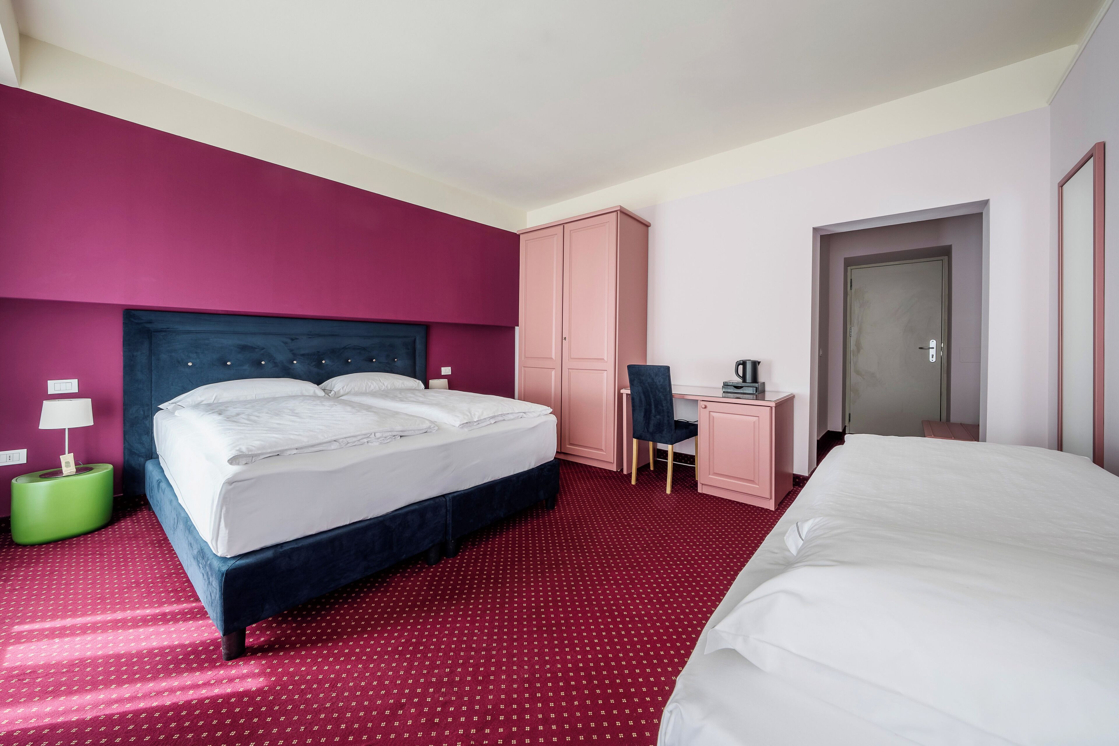 Quarto de hotel com cama, escrivaninha, cadeira, guarda-roupa e porta.