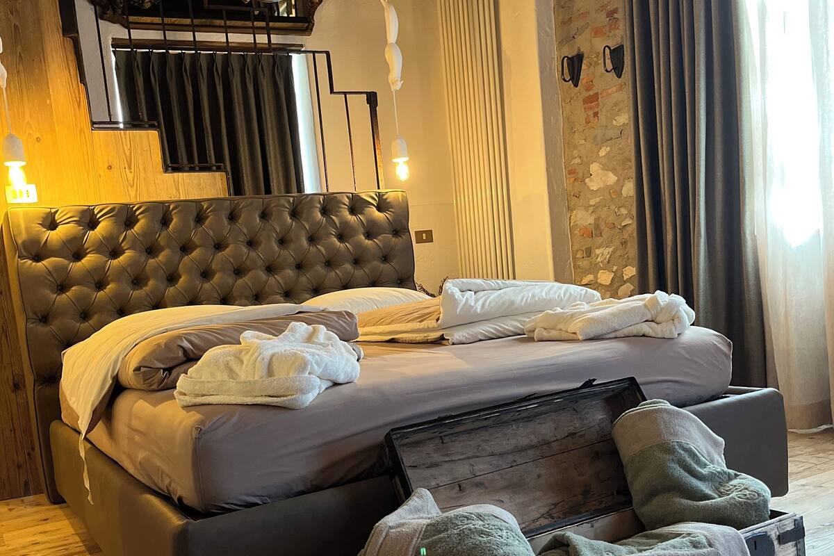 Quarto com cabeceira estofada, cómoda de madeira e uma cama grande com vários travesseiros e cobertores.