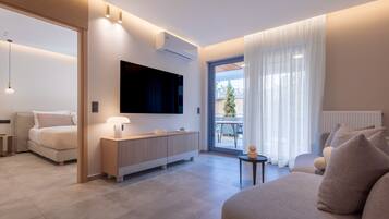 Quarto de hotel moderno com cama, sofá, televisão, mesinha e varanda com vista.