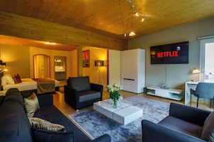 Uma sala de estar moderna com um sofá, poltronas, uma mesa de centro e uma TV exibindo 'NETFLIX'.