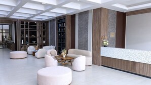 Um lobby moderno com balcão de recepção, área de estar e uma grande porta de vidro que dá para outro espaço.