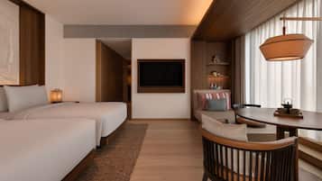 Quarto de hotel com duas camas, uma mesa de jantar, uma televisão e uma janela grande.