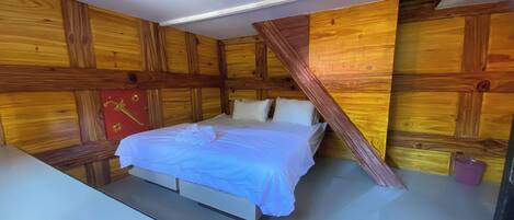 Quarto com cama, paredes de madeira e porta vermelha com emblema dourado.
