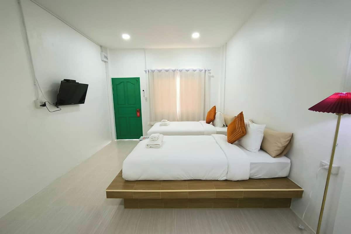 Quarto de hotel com duas camas de solteiro, uma porta verde, uma televisão de tela plana presa à parede e um abajur.