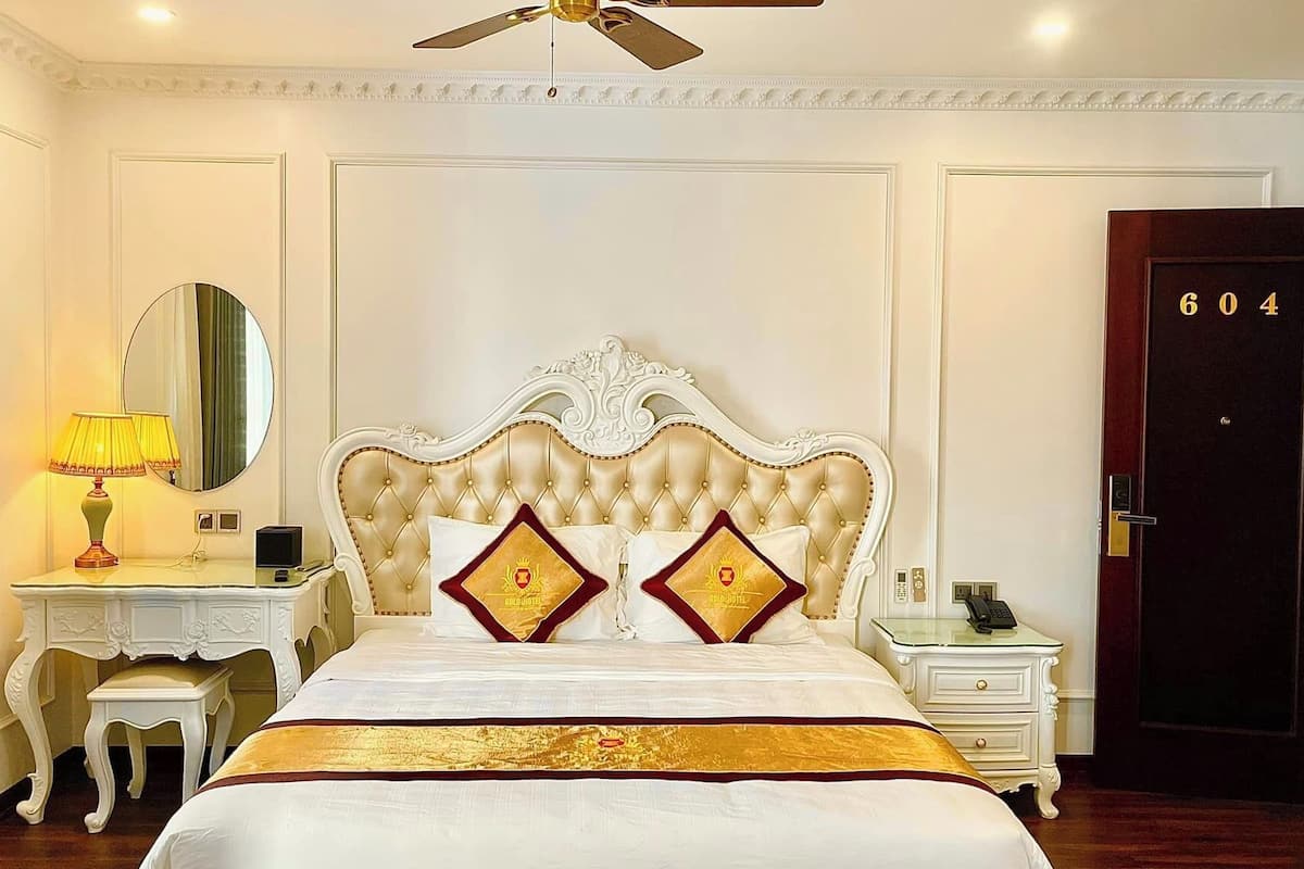 Quarto de hotel com uma cama grande, uma mesa de cabeceira com luminária, um espelho e uma porta com o número 604.