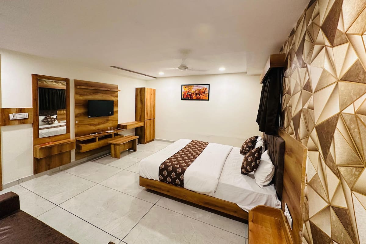 Quarto de hotel moderno com uma cama grande, móveis de madeira, televisão de tela plana e parede com padrão geométrico.
