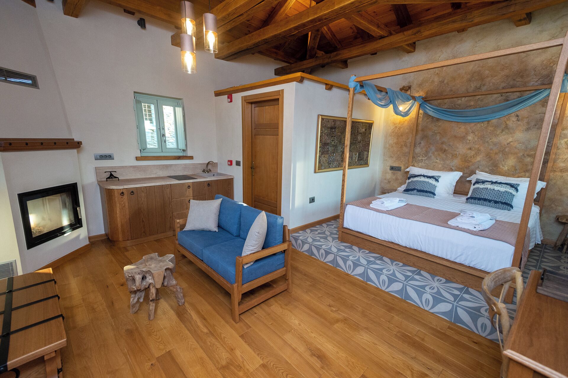 Um quarto aconchegante com teto de madeira, um sofá, uma cama com dossel, uma mesinha e uma janela.
