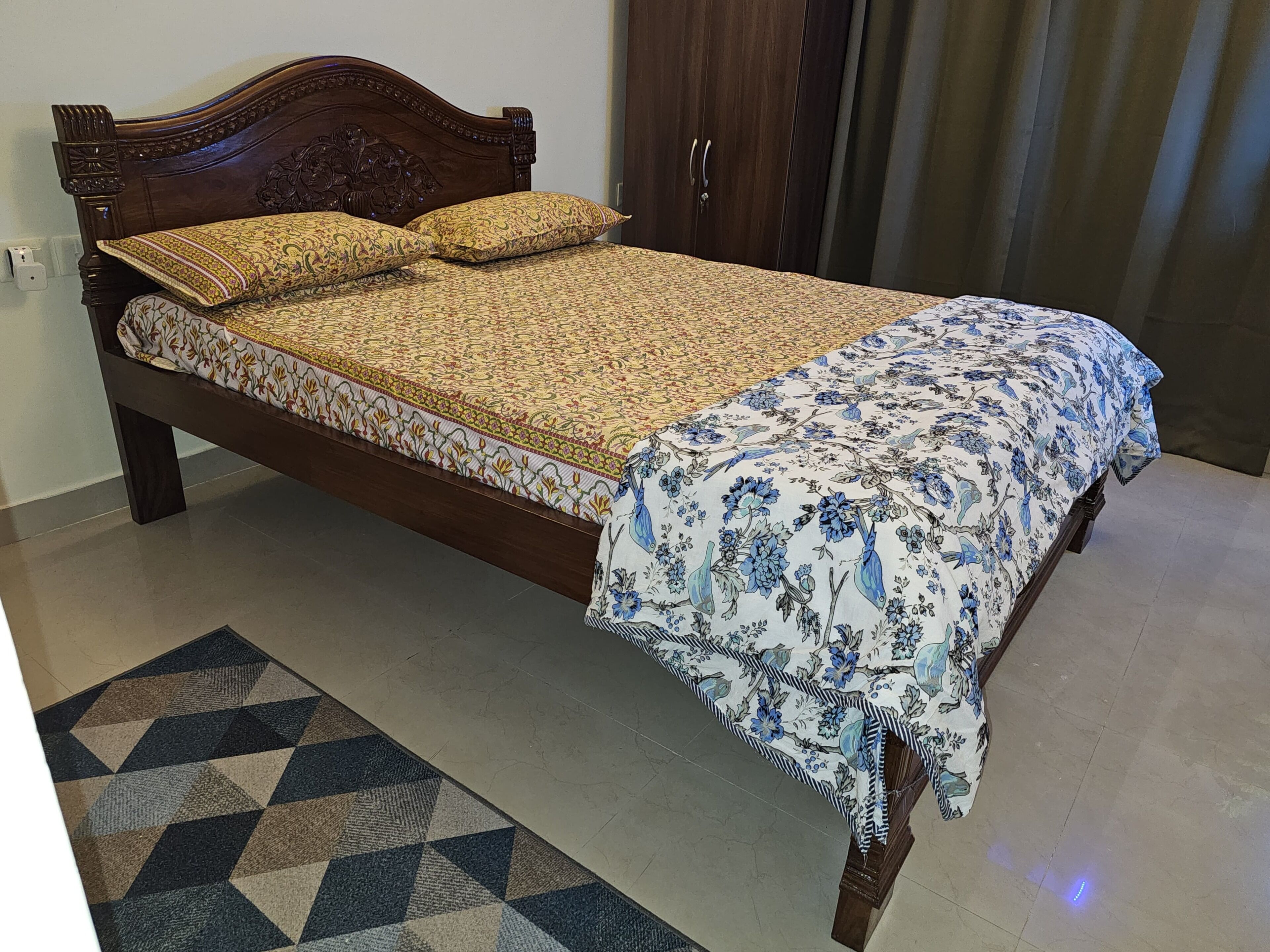 Uma cama com colcha estampada e manta azul florida.
