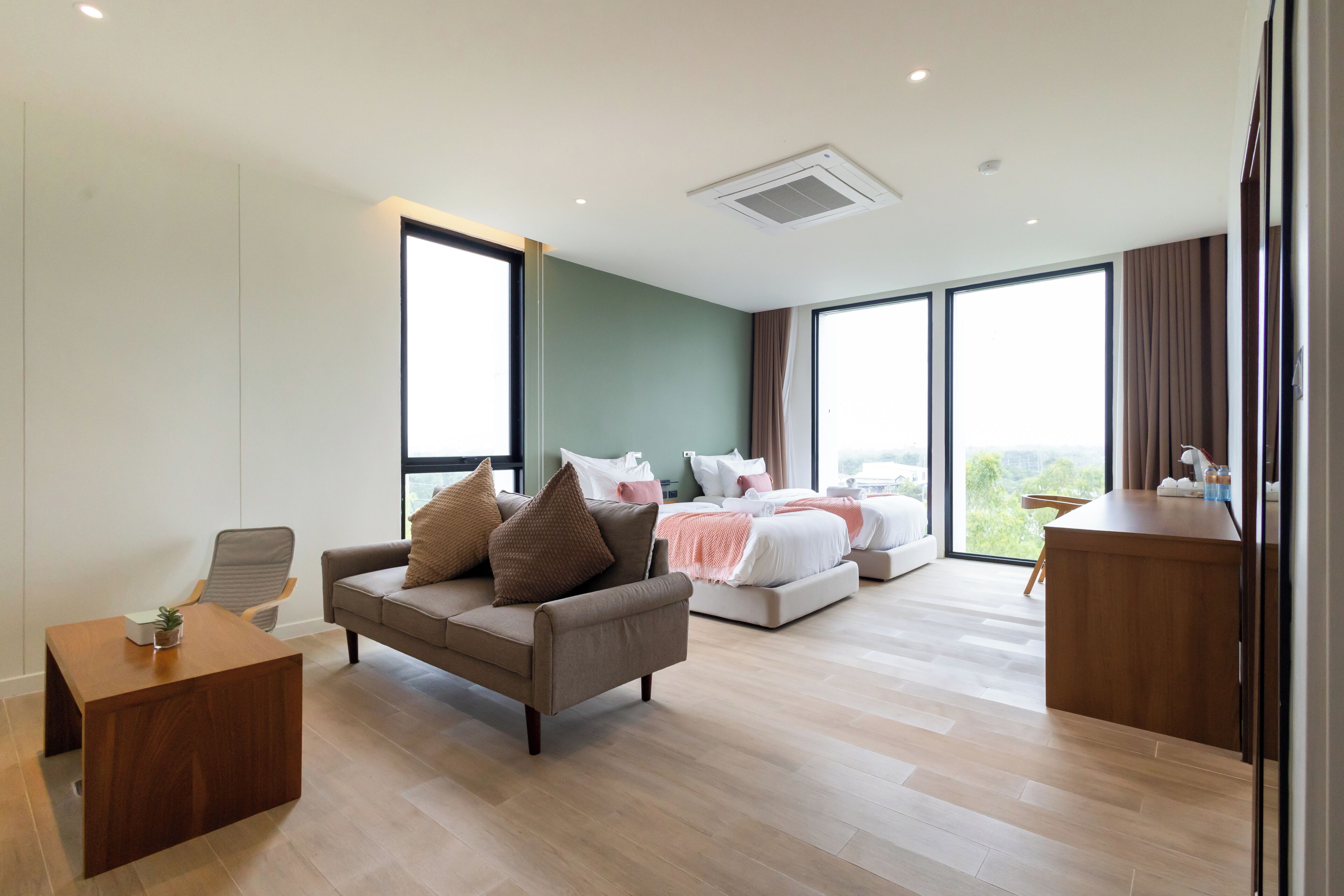 Quarto de hotel moderno com sofá, escrivaninha, cama e amplas janelas com vista.