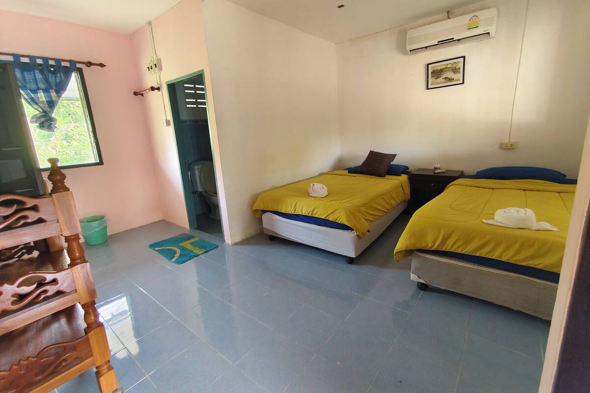 Quarto com duas camas, um armário de madeira, um cesto de lixo verde e um aparelho de ar condicionado.