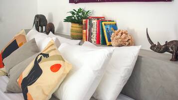 Uma cama com várias almofadas, uma pequena planta, uma pilha de livros e uma pedra decorativa.