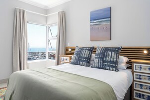 Quarto de hotel com uma cama grande, vista para o mar e paisagem urbana pela janela.