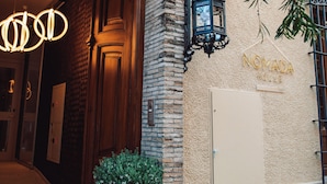 Entrada de um edifício com uma placa indicando 'NOMADA HOUSE', uma planta em vaso e um lança-lume pendurado.