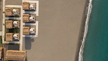 Vista aérea de um hotel à beira-mar com guarda-sóis e mesas de palha, uma praia de areia e o oceano.