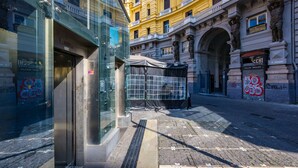 Rua com entrada de edifício, porta de vidro e barreira de metal.