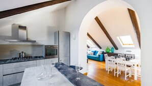Cozinha moderna com bancada de mármore, eletrodomésticos de aço inoxidável e área de jantar com mobiliário branco.