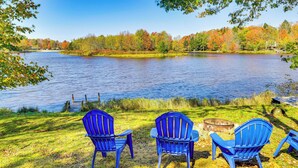 Vista para o lago com três cadeiras Adirondack azuis e uma lareira.