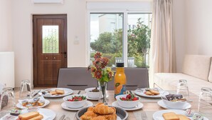 Disposição para o pequeno-almoço com croissants, fruta e sumo numa mesa com vista para o exterior verde.