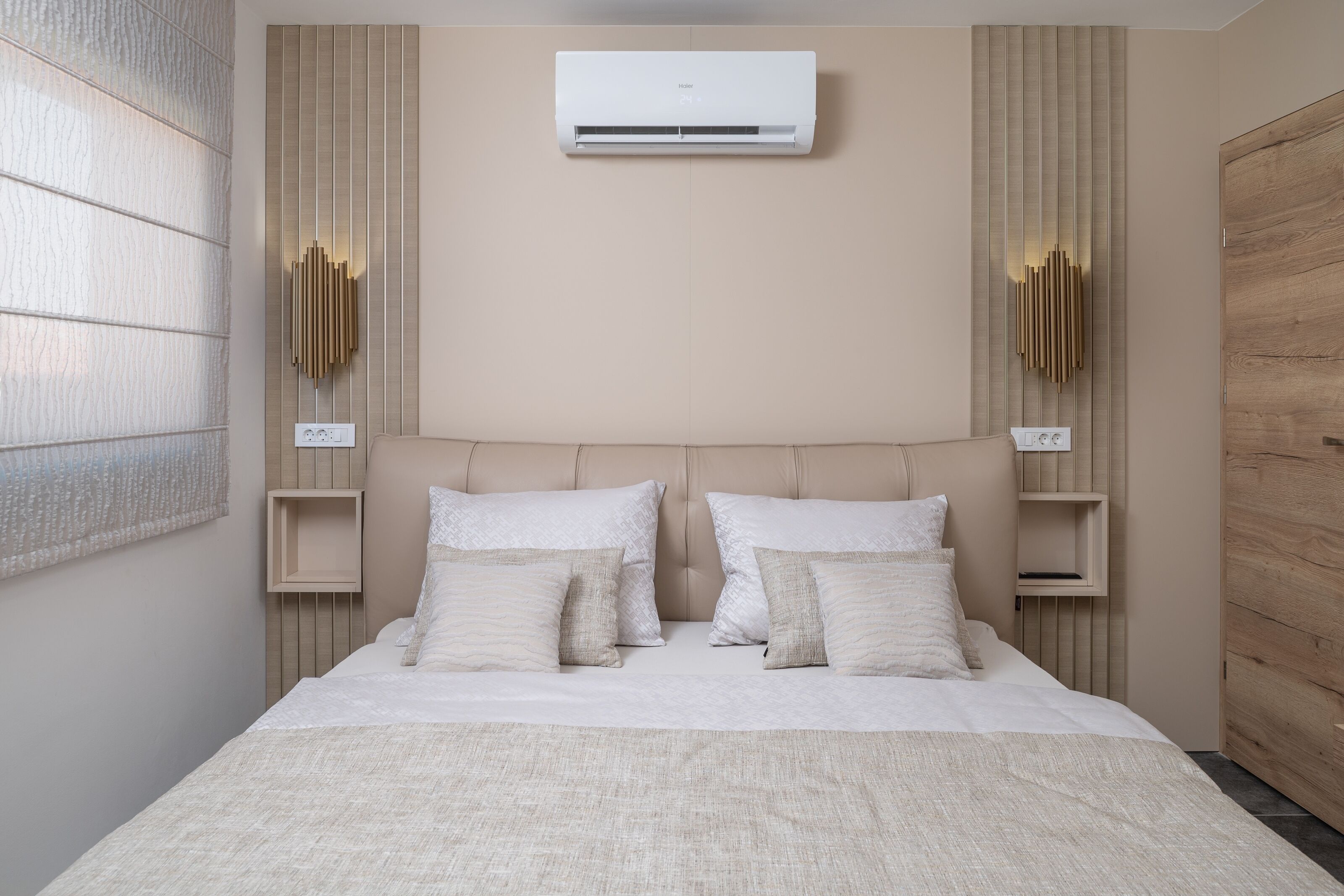 Quarto moderno com uma cama grande, duas mesas de cabeceira, ar condicionado fixado na parede e um guarda-roupa de madeira.