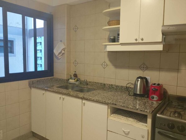 Uma cozinha com bancada de granito, pia, chaleira, torradeira e fogão.
