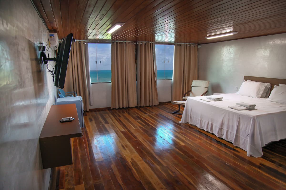 Quarto com cama, escrivaninha, cadeira, televisão e janela com cortinas.
