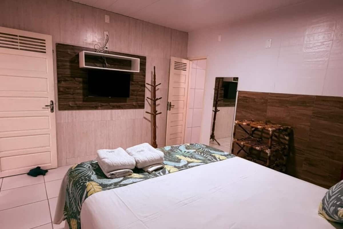 Quarto com cama, televisão fixada na parede, cabeceira de madeira e espelho.