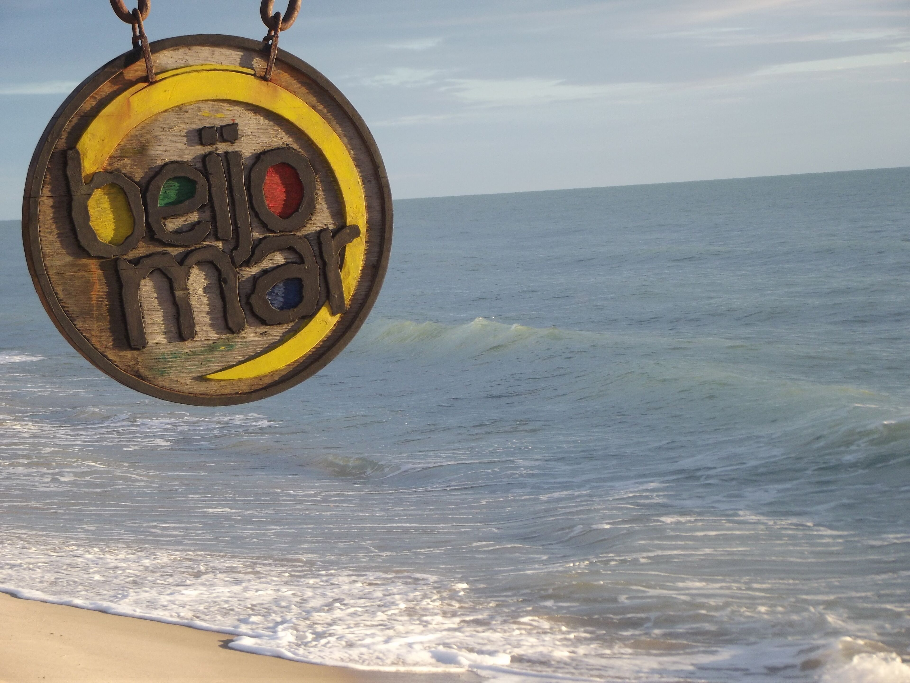Uma placa de madeira com a inscrição 'bello mar' suspensa sobre o oceano.