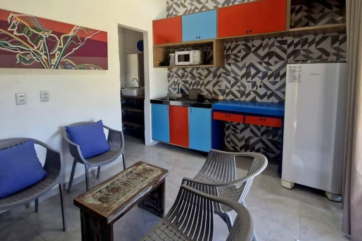 Um espaço de estar compacto com cozinha compacta, área de refeições com banco e sala de estar com cadeiras.