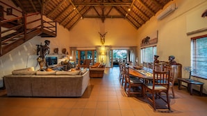 Uma sala de estar ampla, com teto de madeira alto, lareira, mesa de jantar com cadeiras e escada.