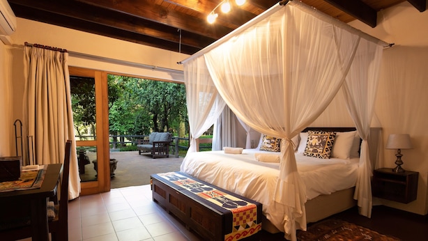 Quarto com cama de dossel, um banco de madeira, uma mesa e vista para o exterior.