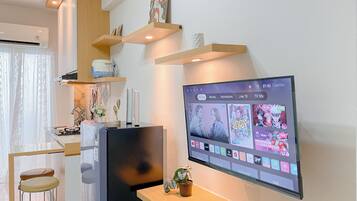 Sala de estar moderna com TV de tela plana na parede, área de cozinha com fogão e espaço para refeições com um banco alto.