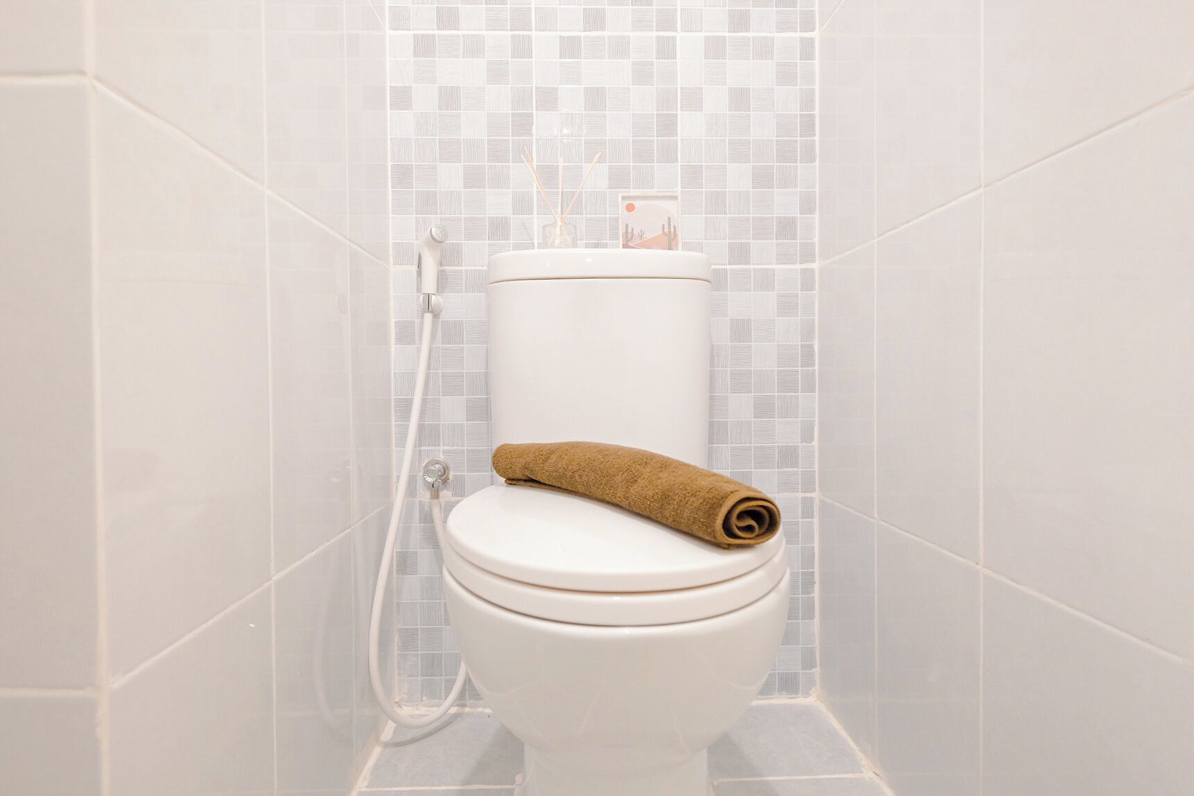 Casa de banho com rolo de papel toalha castanho em cima, um chuveiro e parede com pequenos azulejos quadrados.