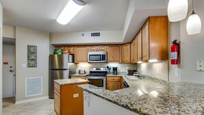 Uma cozinha moderna com bancadas de granito, eletrodomésticos de aço inoxidável, armários de madeira e iluminação pendente.