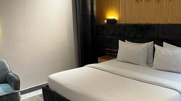 Quarto de hotel moderno com uma cama grande, uma mesinha de cabeceira, uma cadeira e ar condicionado fixado na parede.