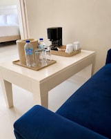 Quarto de hotel com uma cama, cafeteira, garrafas de água, copos e uma bandeja com xícaras.