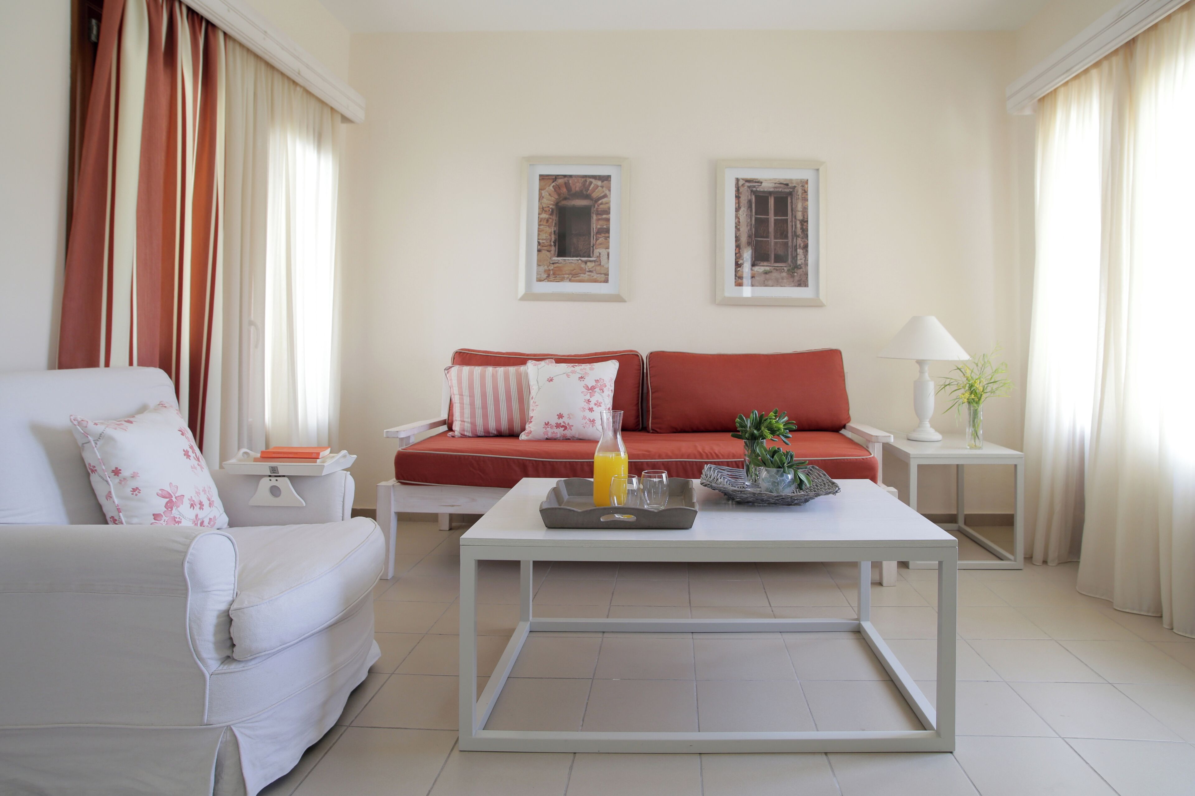 Uma sala de estar moderna com um sofá branco, um sofá vermelho, uma mesa de centro e uma pequena mesa lateral com um abajur e uma planta.