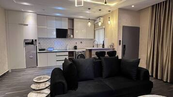 Uma sala de estar moderna com um sofá preto, uma mesa de centro e um espaço de jantar com uma mesa pequena e cadeiras.