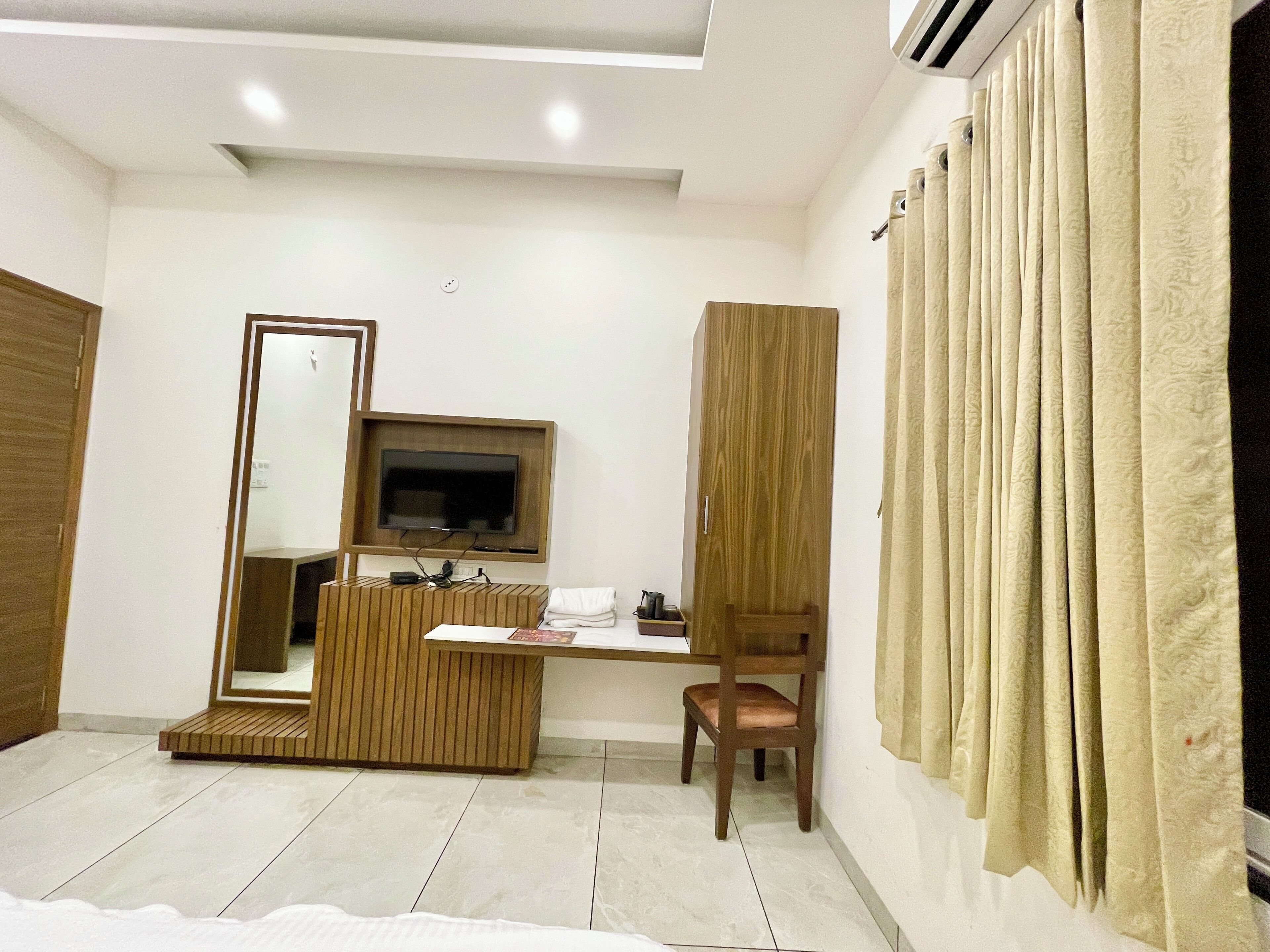Quarto de hotel moderno com escrivaninha de madeira, televisão, espelho e guarda-roupa.