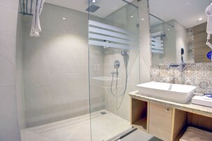 Uma casa de banho moderna com cabine de duche em vidro, lavatório branco e espelho sobre bancada.