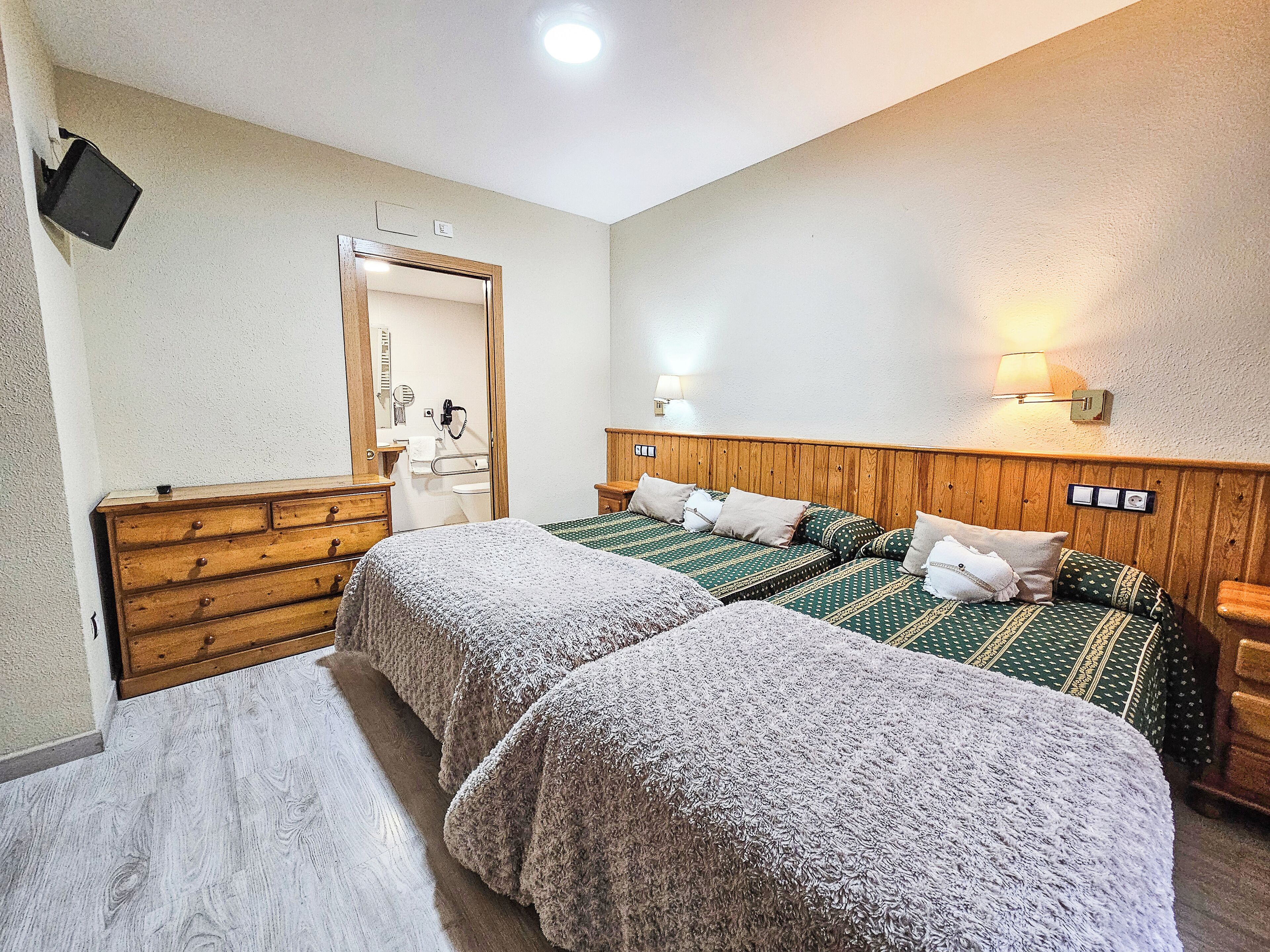 Quarto com duas camas, cabeceiras de madeira, um espelho, mesa de cabeceira e luminária na parede.